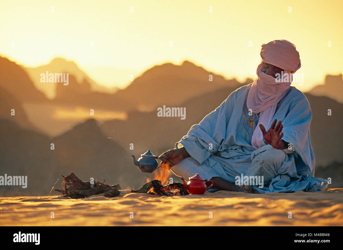 Algeria. Near Djanet. Sahara desert. Man of Tuareg tribe making tea on ...
