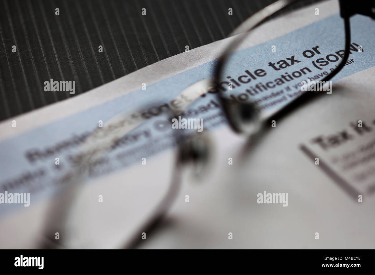 Man's glasses sit on top of newspaper with lens focusing on word tax ...