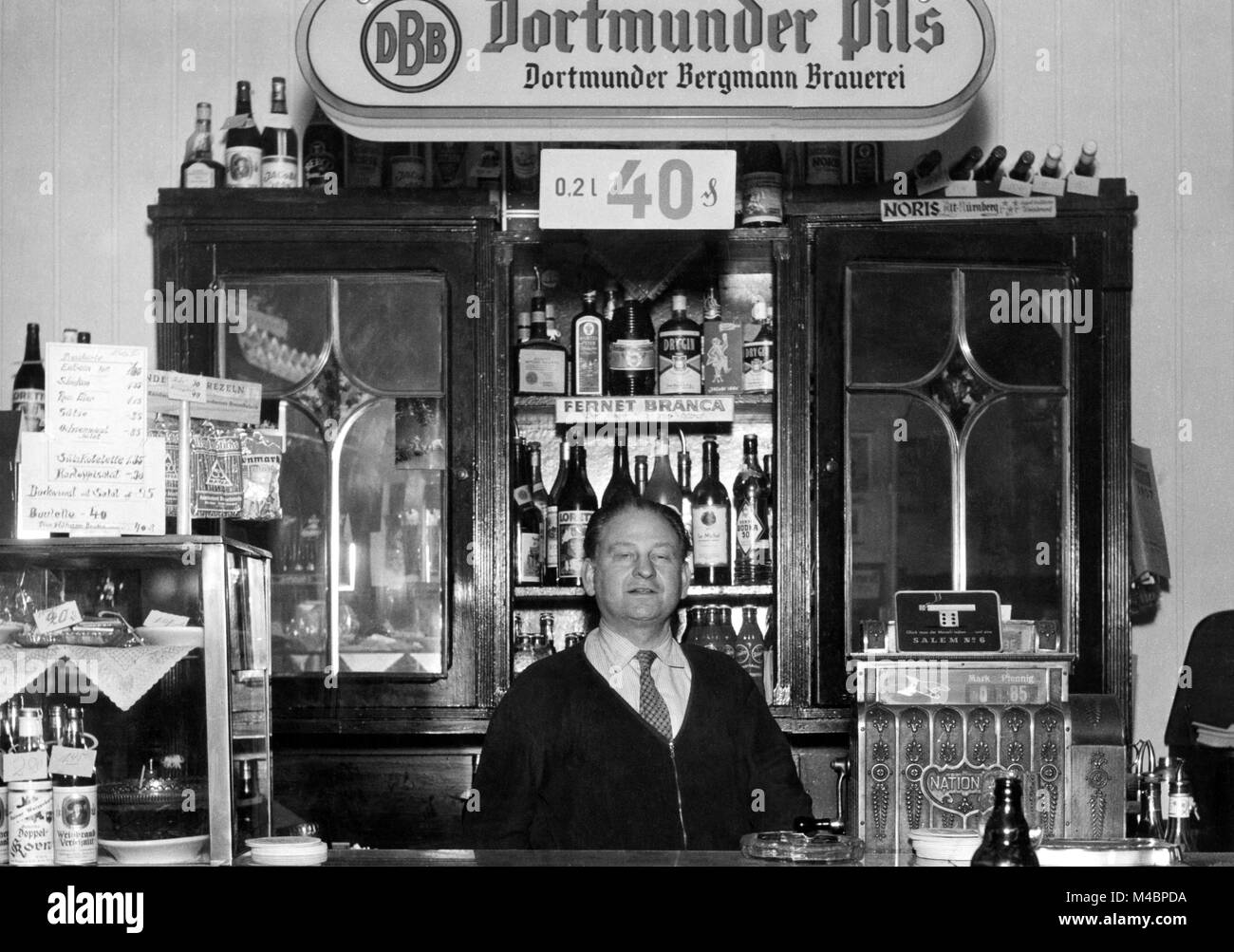 Innkeeper stands behind the bar of a pub,1960s,exact place unknown ...
