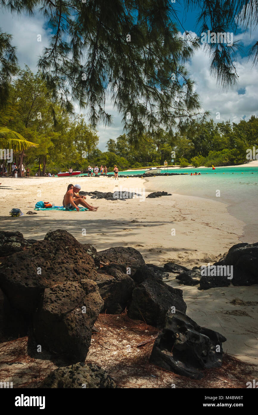Tourists framed by filao trees relaxing on the beach of l'Ile aux Cerfs ...
