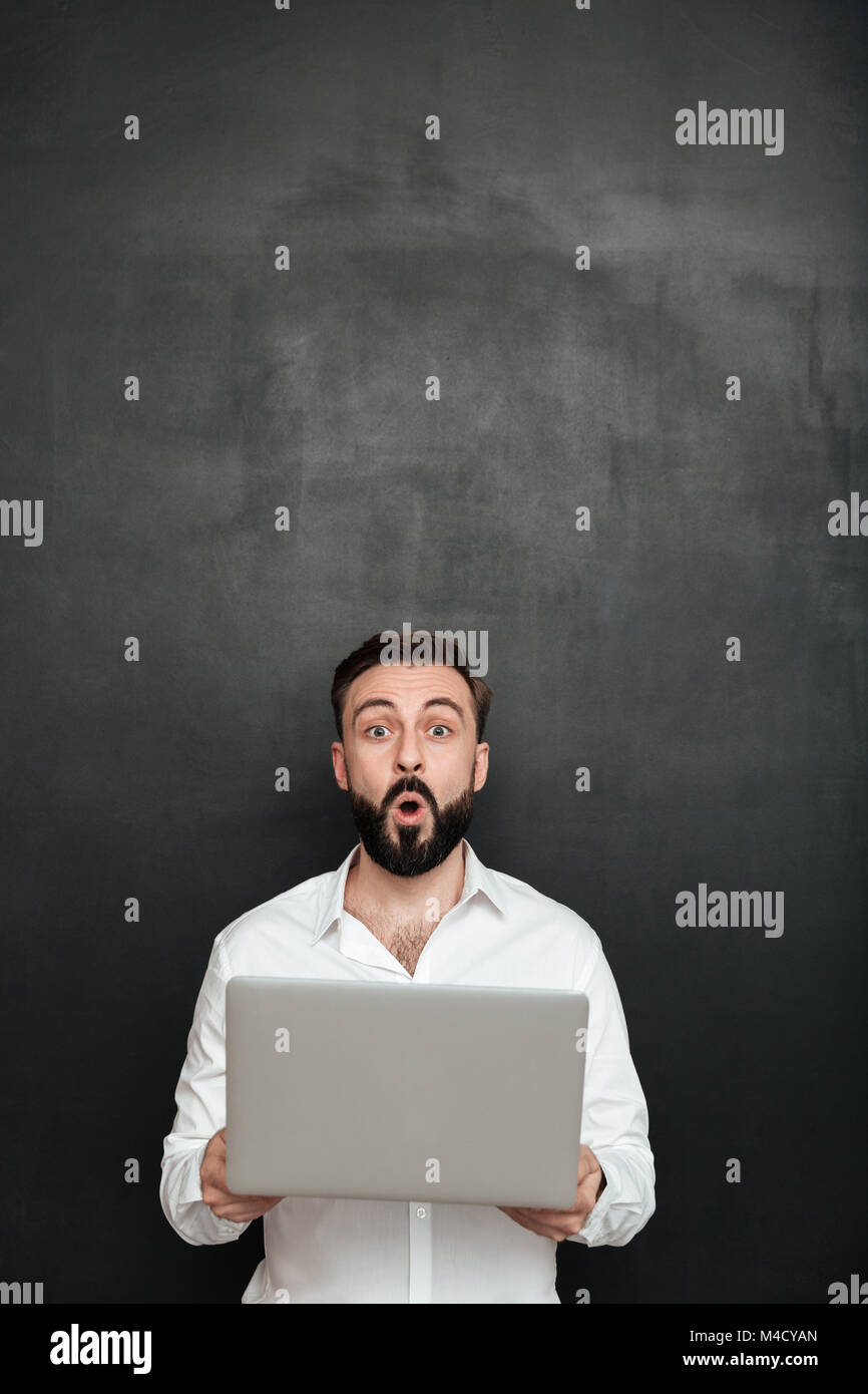 Image of excited bearded man holding silver personal computer and ...