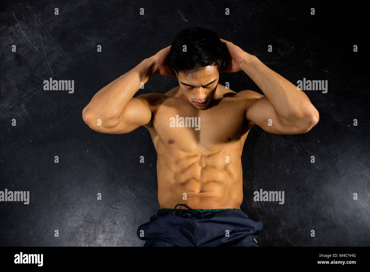 An Asian muscular fitness model performing abdominal crunches. Overhead ...
