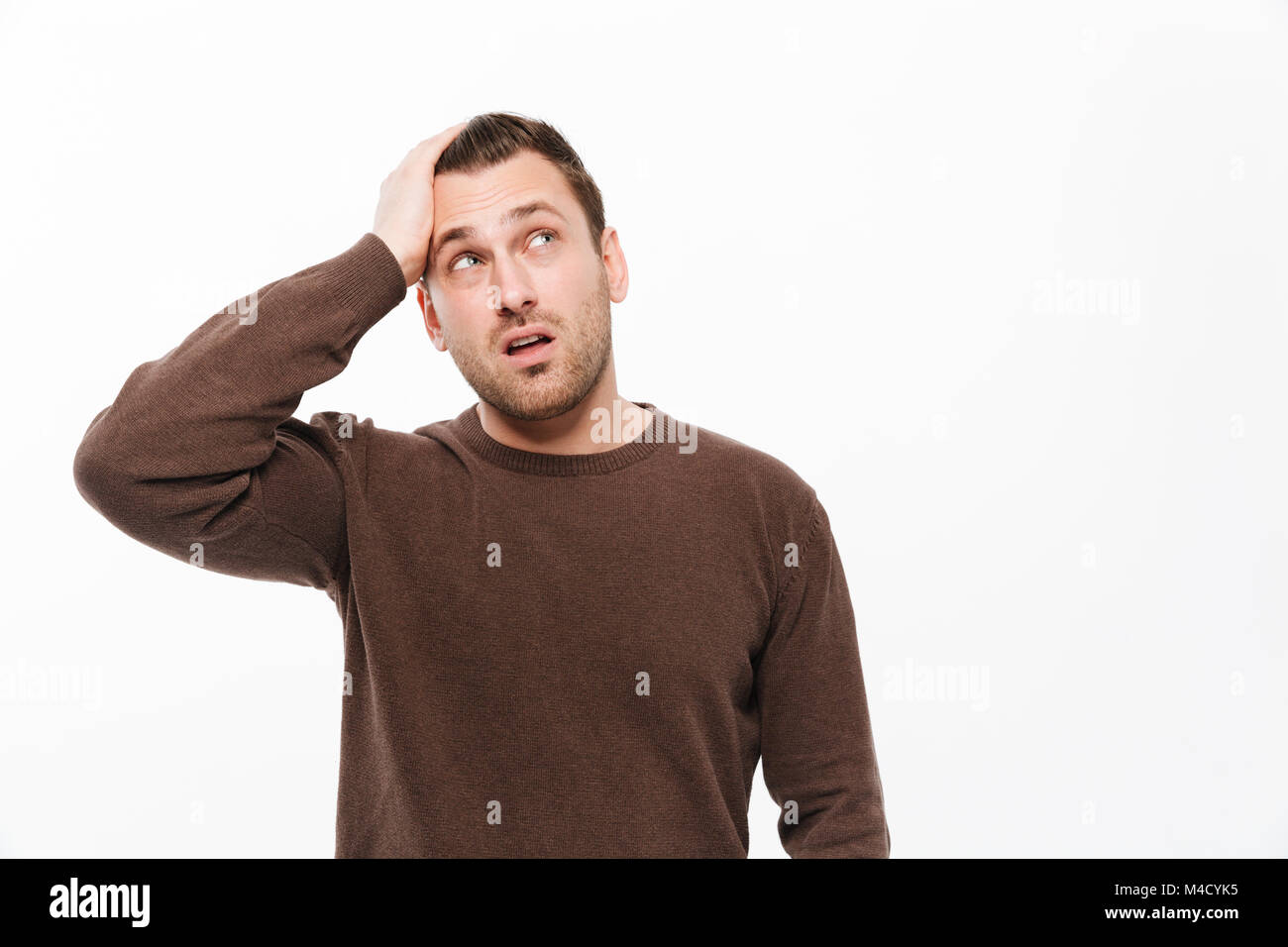 Photo of confused young man standing isolated over white background ...