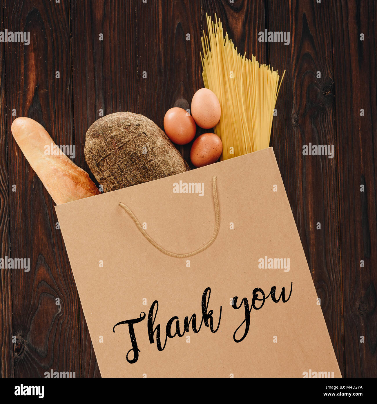 top view of bread, pasta and eggs in paper bag with words thank you ...