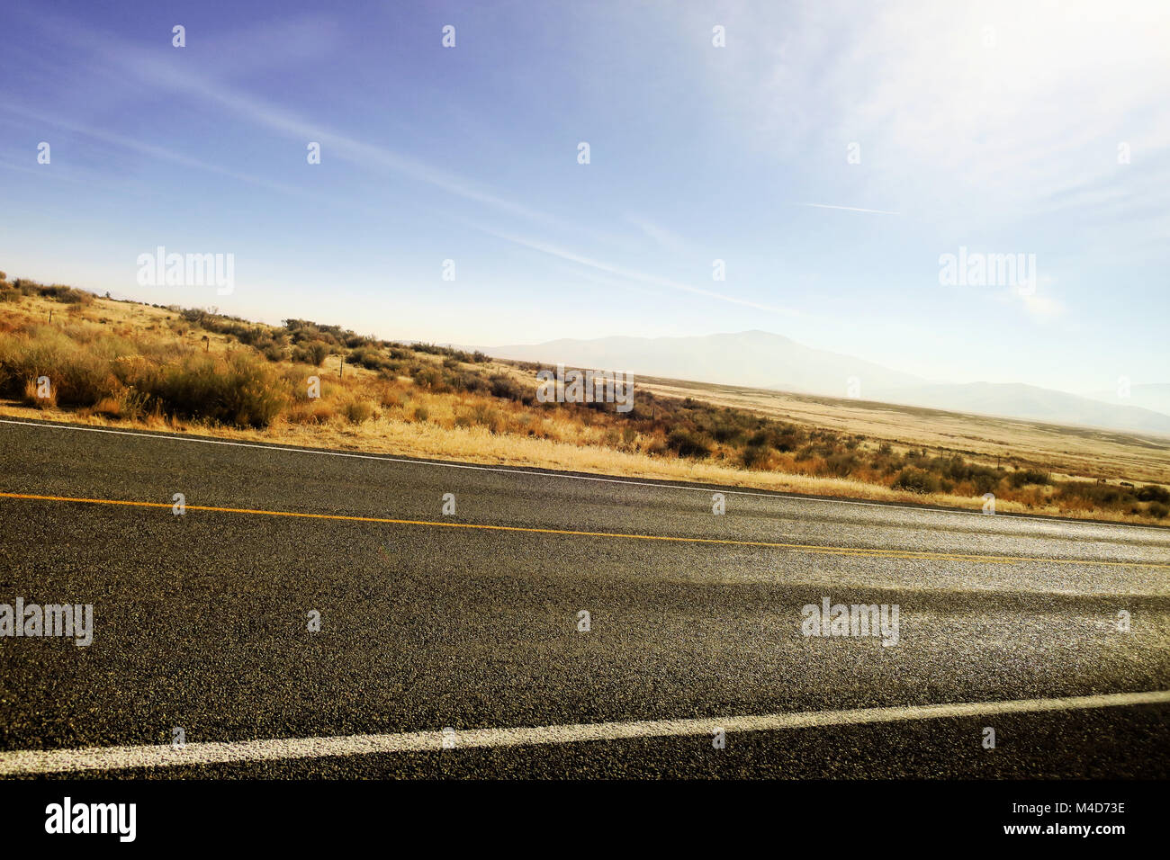 An angled road in the Utah desert with cirrus clouds floating high up ...