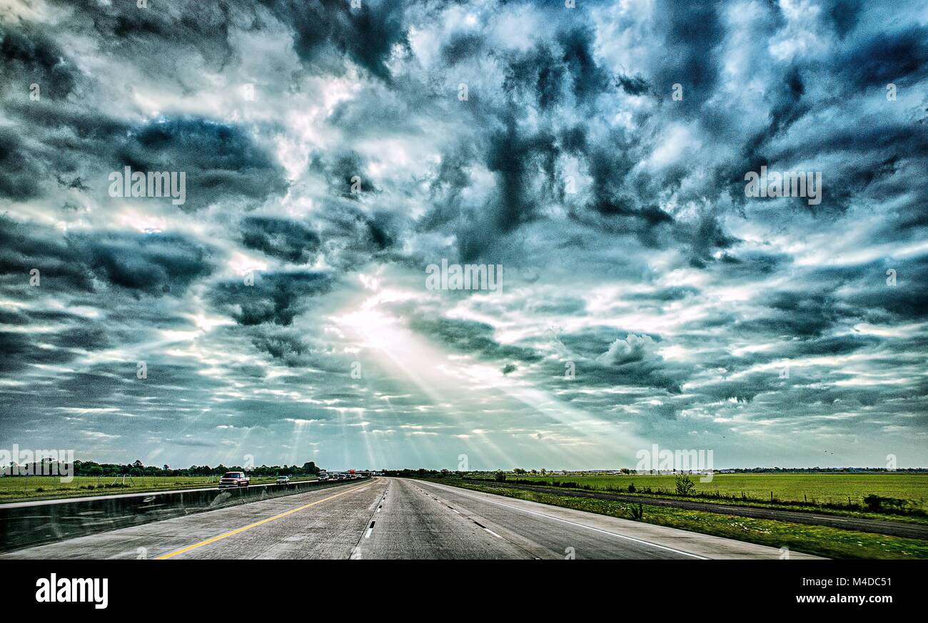 freeway through country landscape with dramatic skyes and sun rays ...
