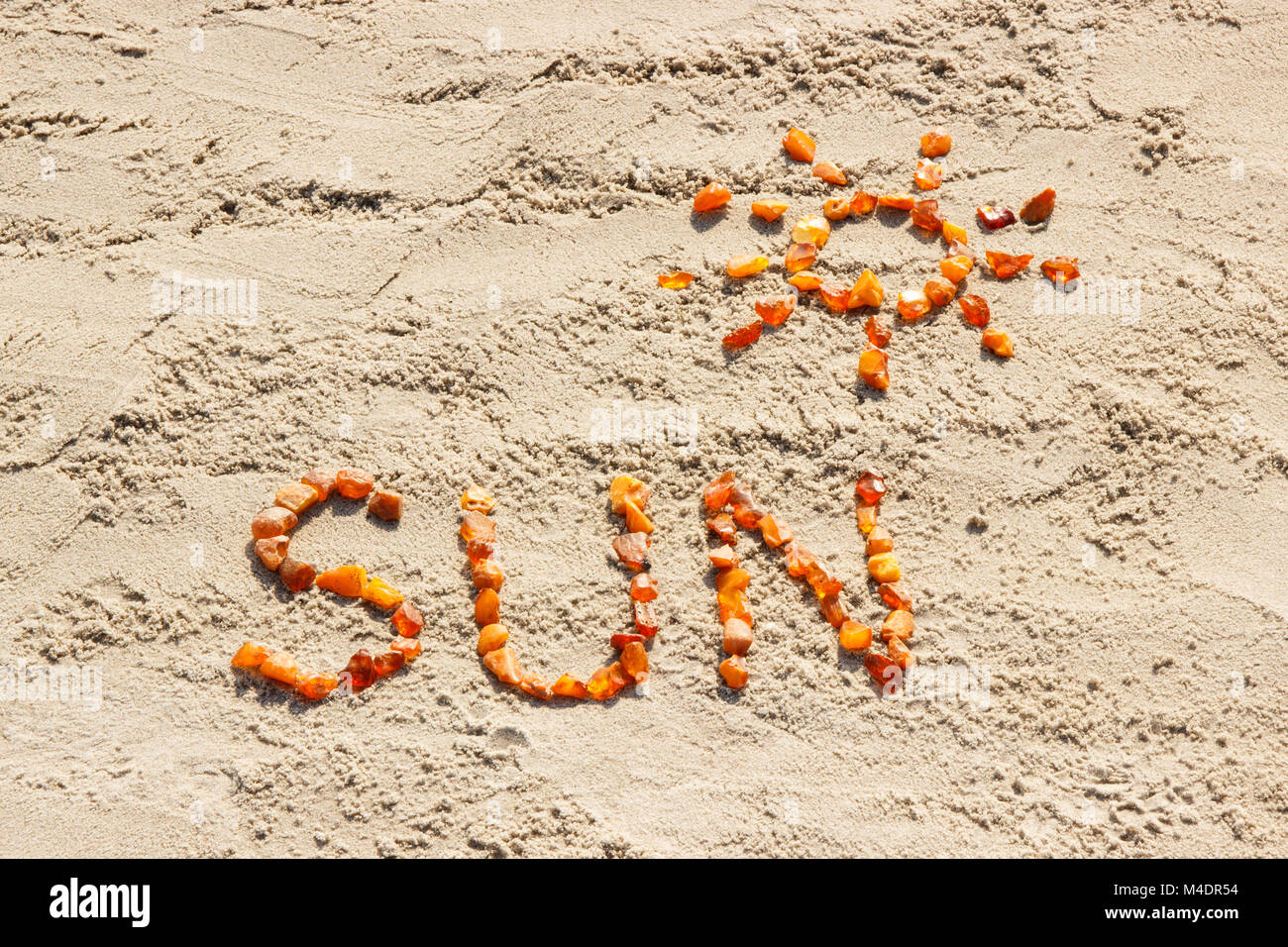 Inscription sun and shape of sun made of amber stones on sand at beach ...