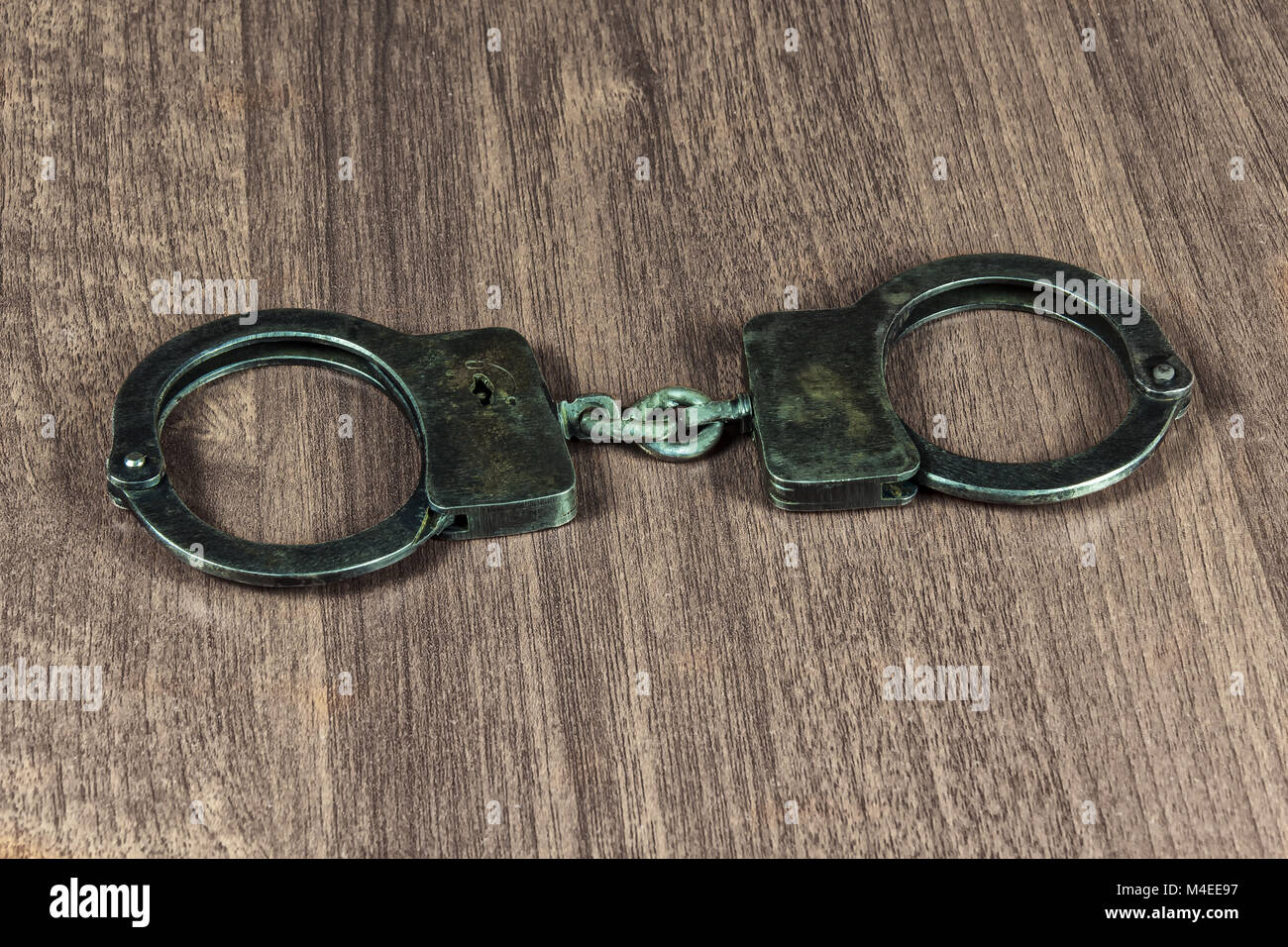 Metal handcuffs lie on a wooden table Stock Photo - Alamy