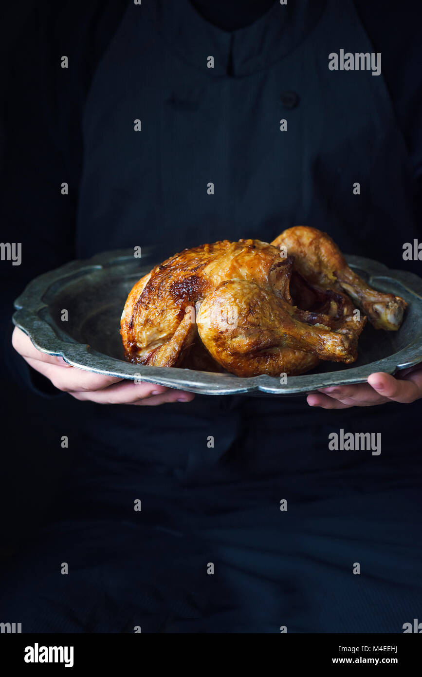 Person holding a Roast chicken on a pewter plate Stock Photo - Alamy