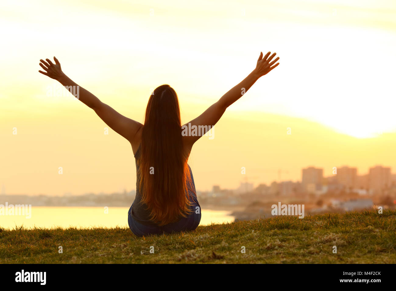 Back view backlight portrait of a single cheerful woman raising arms ...