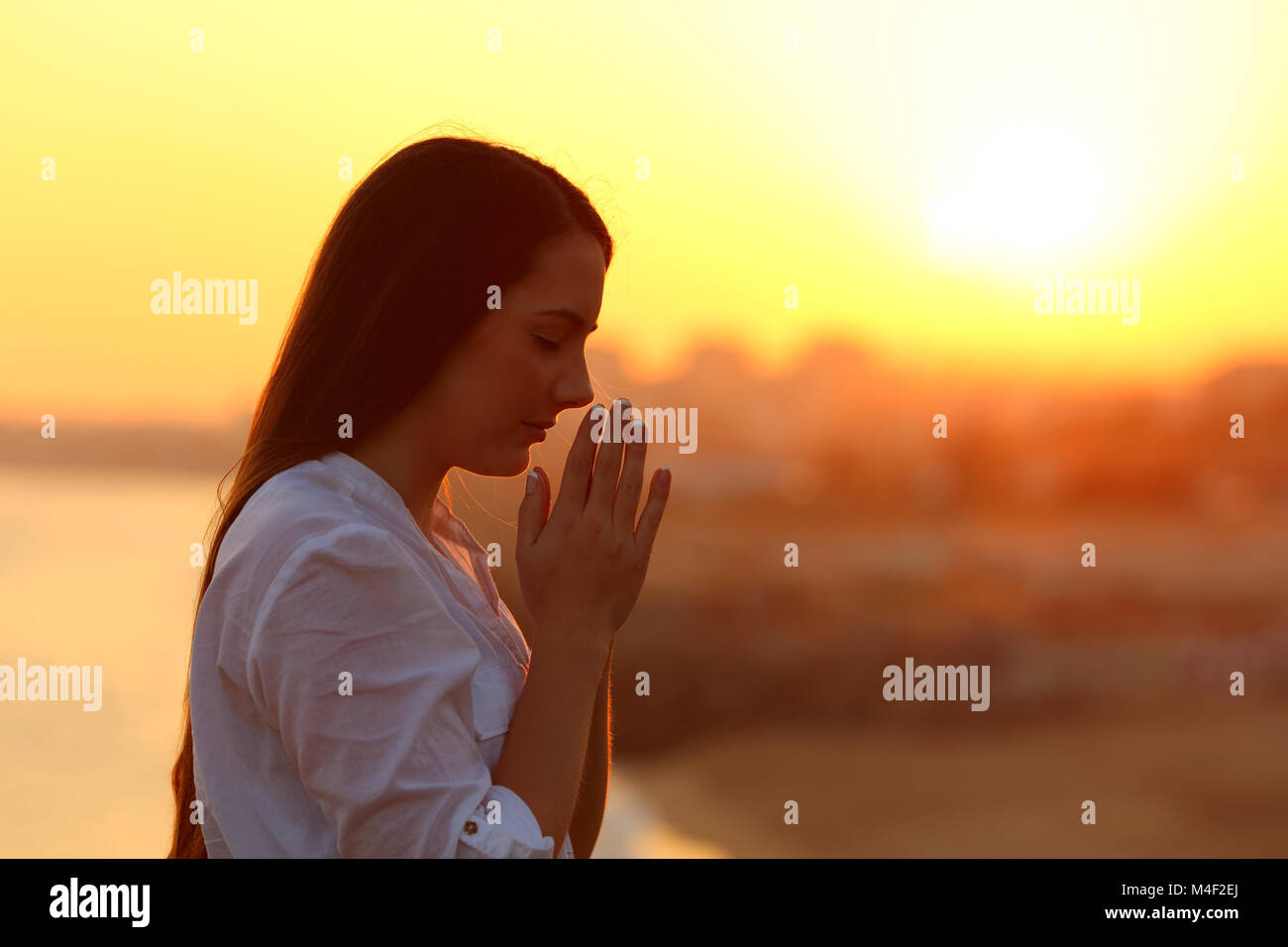 Side view backlight portrait of a single woman praying and looking down ...