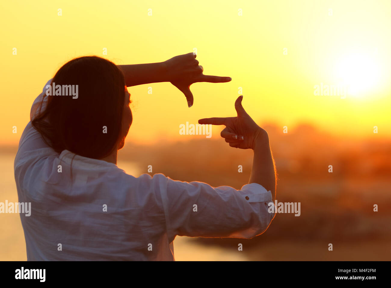 Back view backlight portrait of a woman framing with fingers at sunset ...