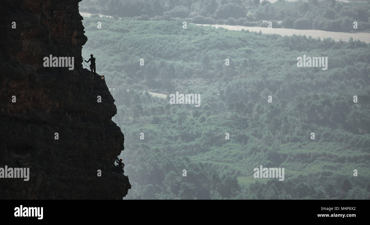 Climbers hanging by a cliff edge against land Stock Photo - Alamy