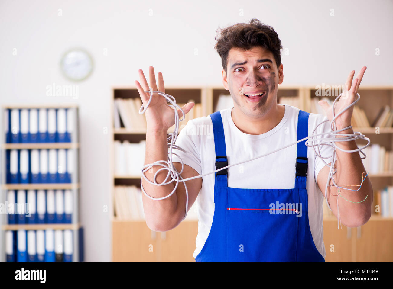 Funny young electrician tangled in cables Stock Photo - Alamy