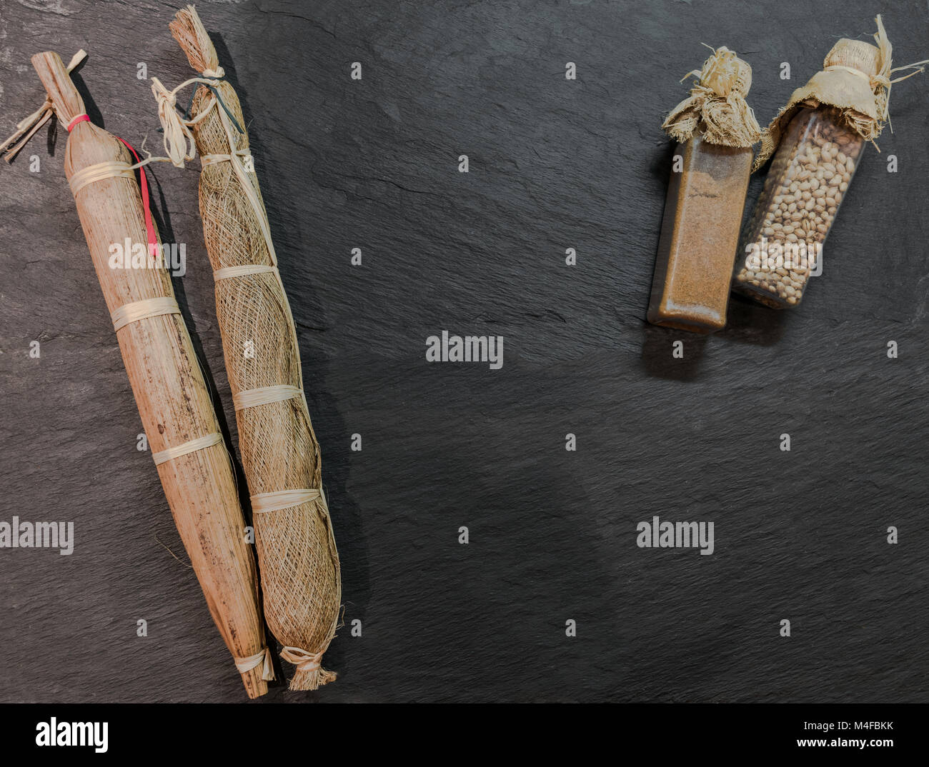 Spices in the bottles and rolled in palm tree bark placed on black rock ...