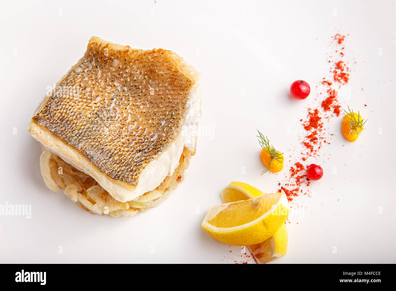 cooked fish fillet of pike-perch on a bed of onion served with a lemon ...