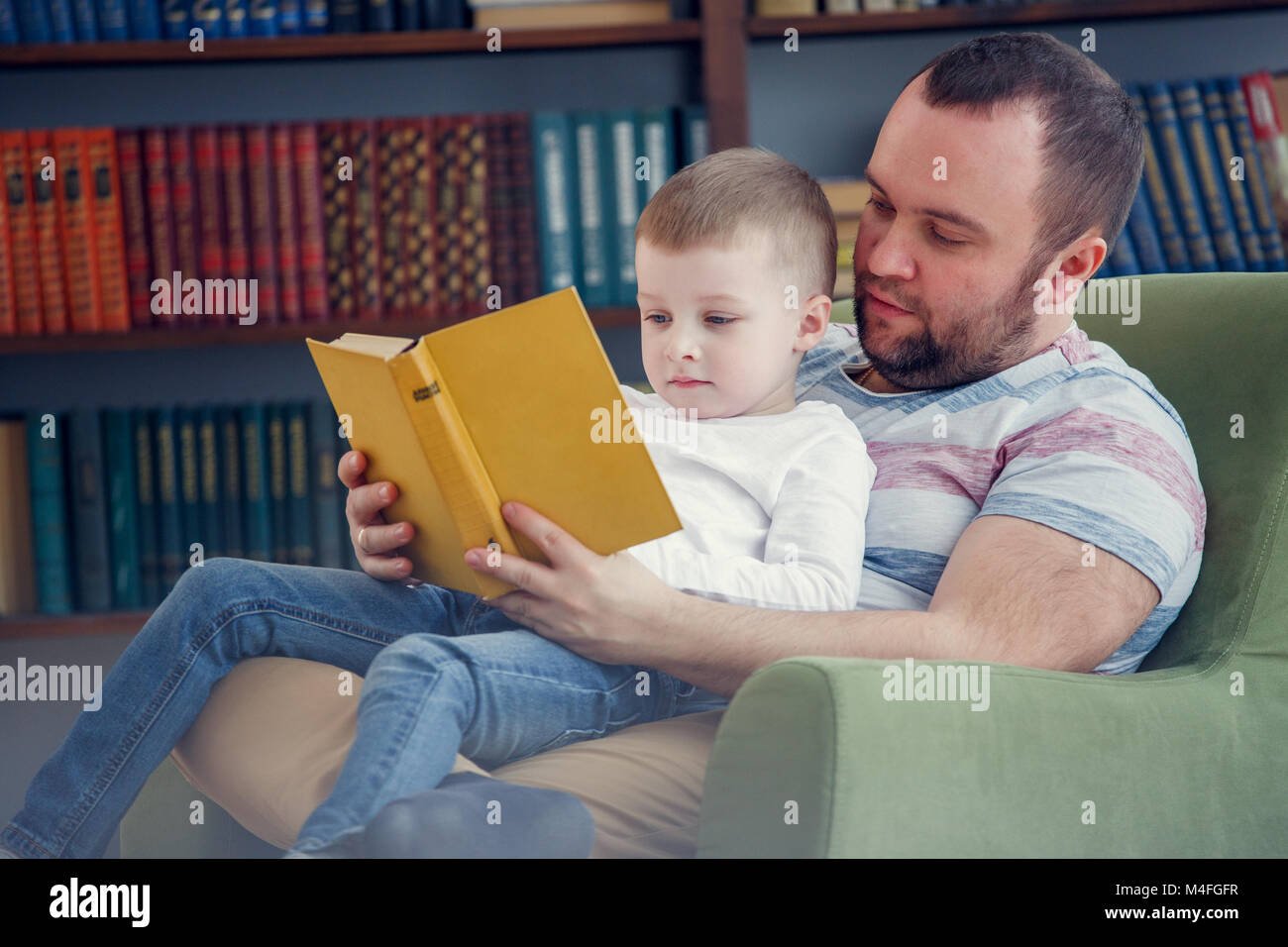Photo of dad reading to son book sitting in chair at apartment Stock ...