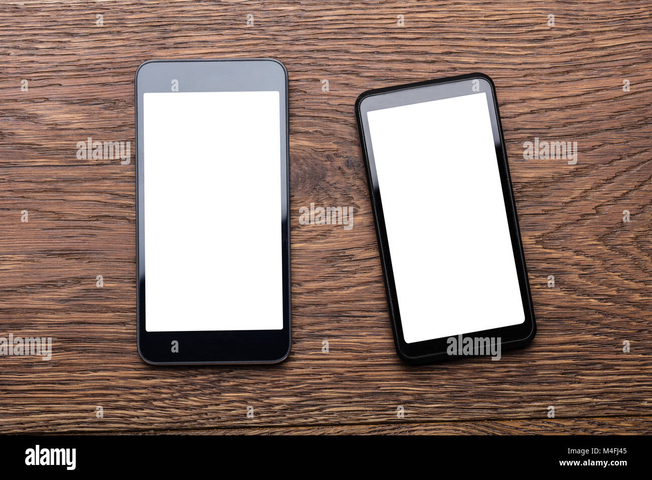 High Angle View Of Two Mobile Phones Showing Blank Screen On Wooden ...