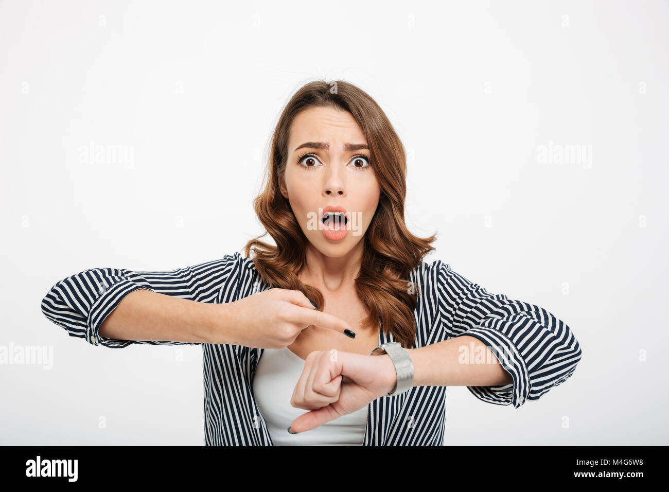 Portrait of a scared casual girl pointing at her wristwatch isolated ...