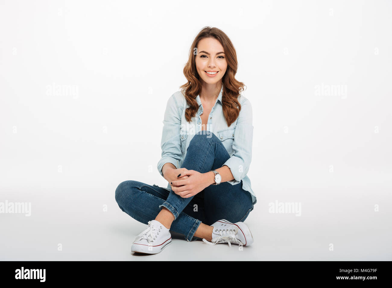 Photo of cheerful young woman sitting isolated over white wall ...
