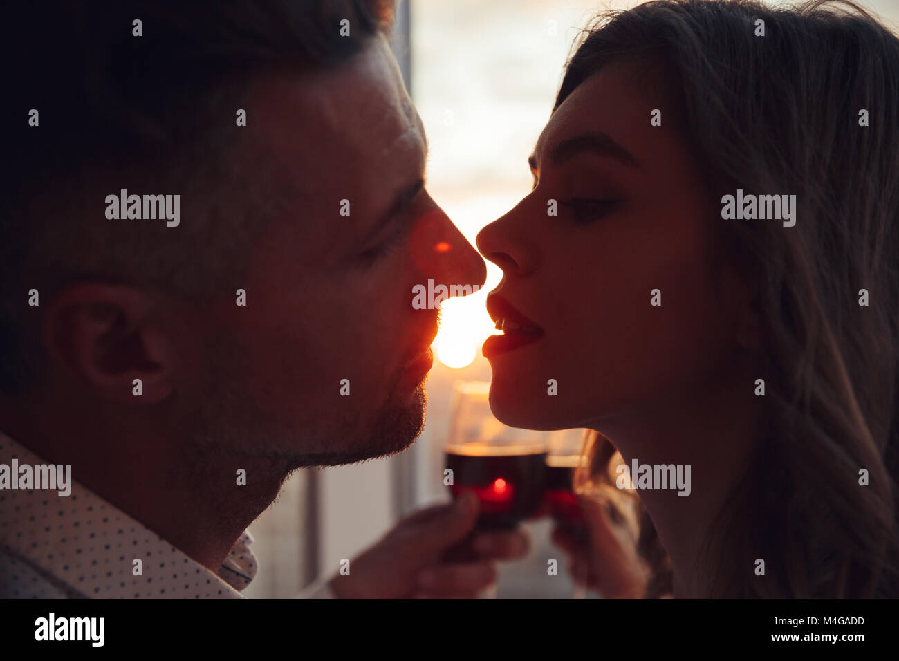 Portrait of young beautiful lovers kissing at sunset and holding glass ...