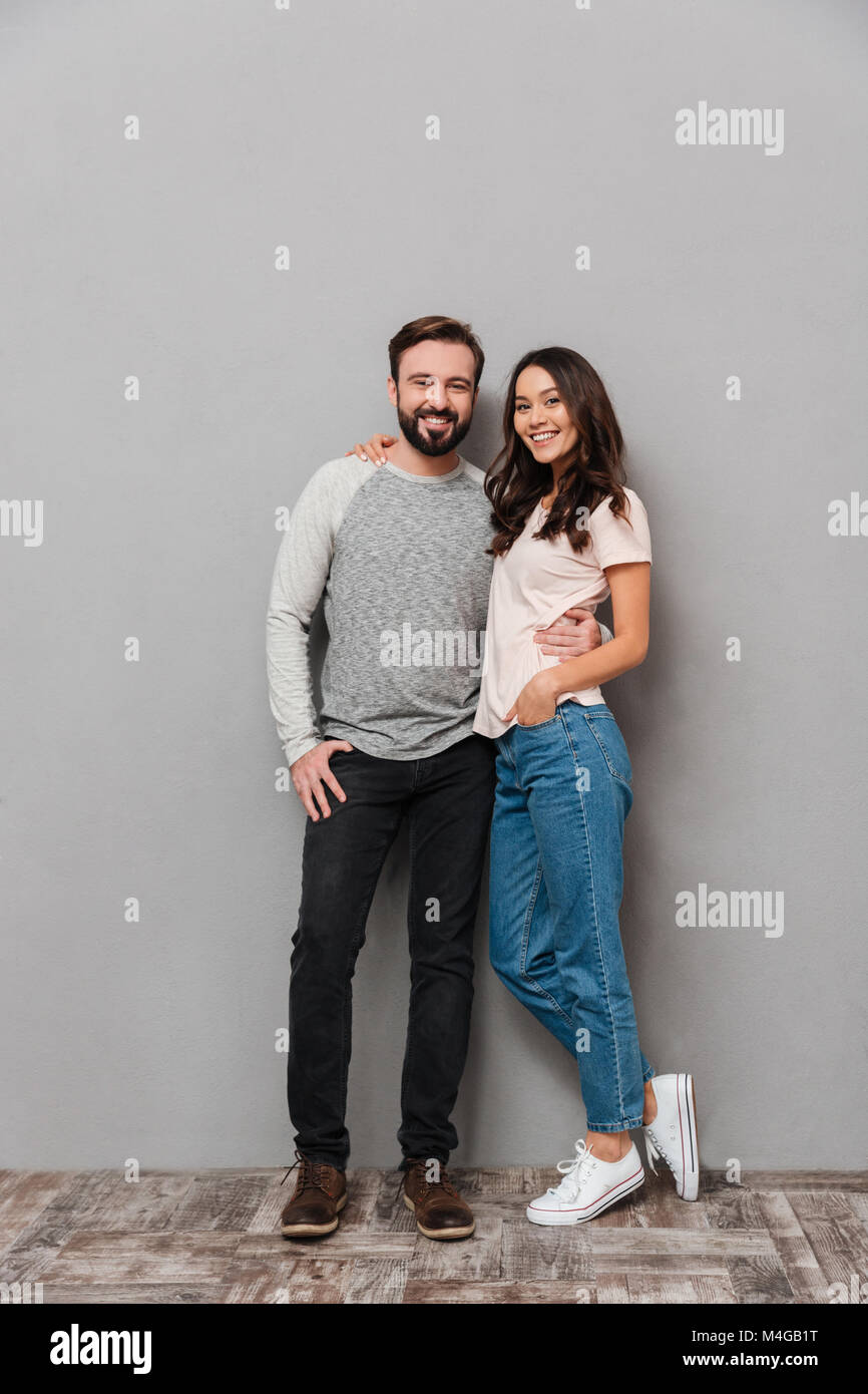 Full length portrait of a cheerful young couple hugging and looking at ...