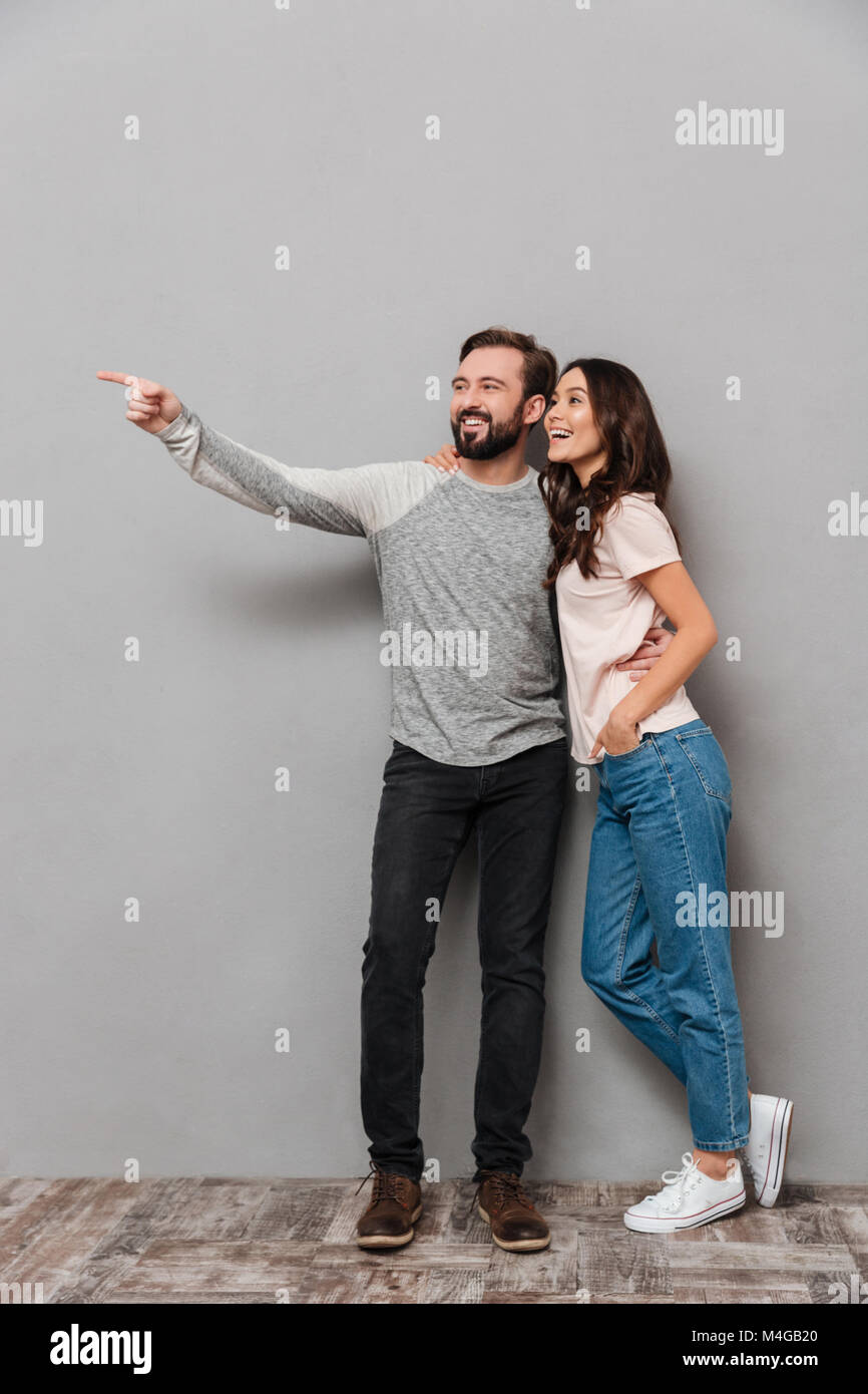 Full length portrait of a cheerful young couple hugging and pointing ...