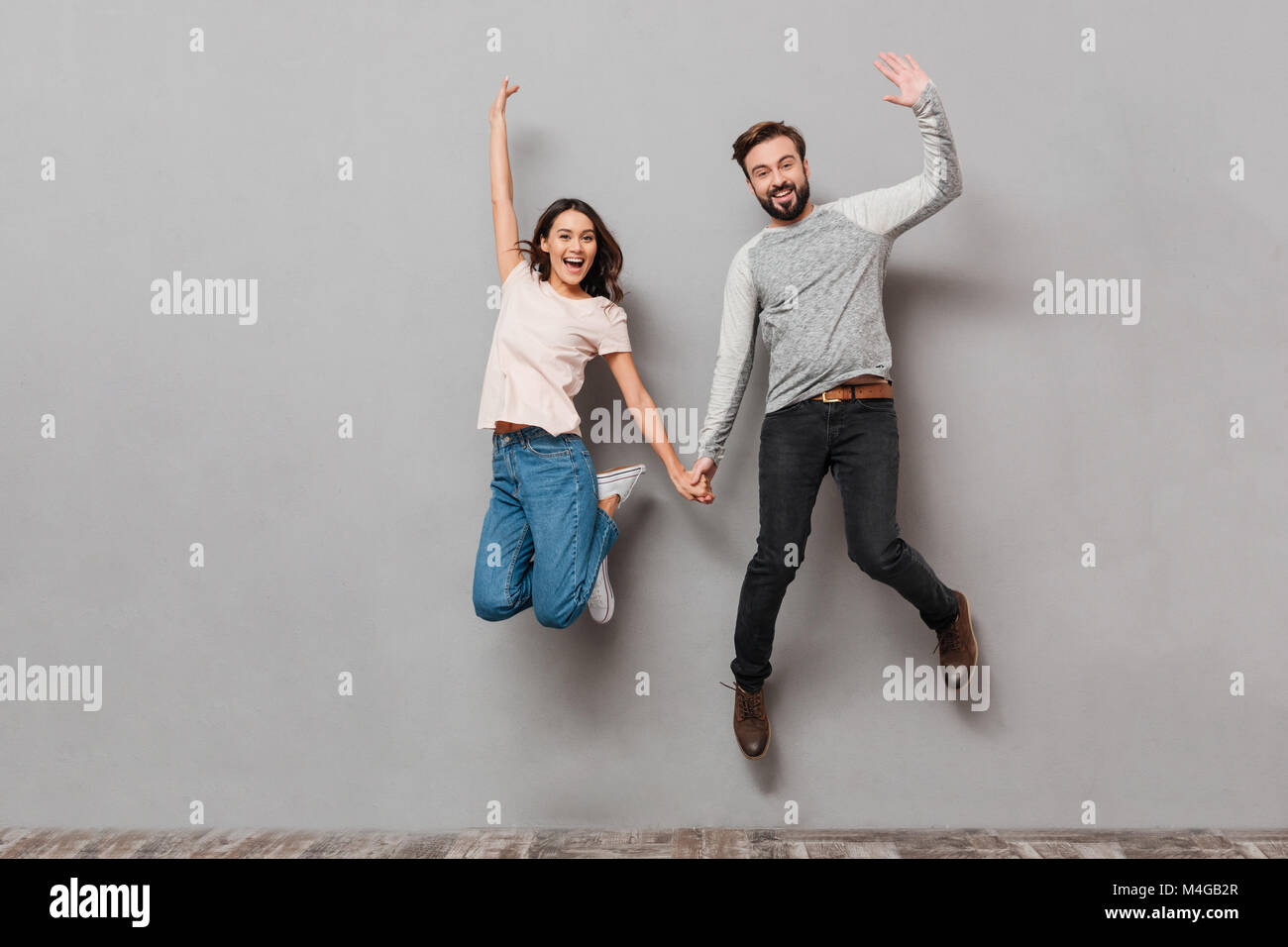 Full length portrait of a cheerful young couple jumping together with ...