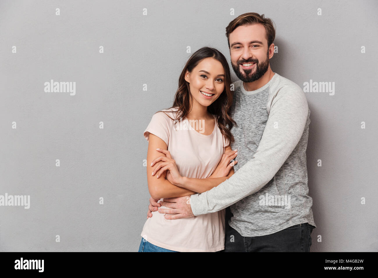 Portrait of a smiling young couple hugging and looking at camera over ...