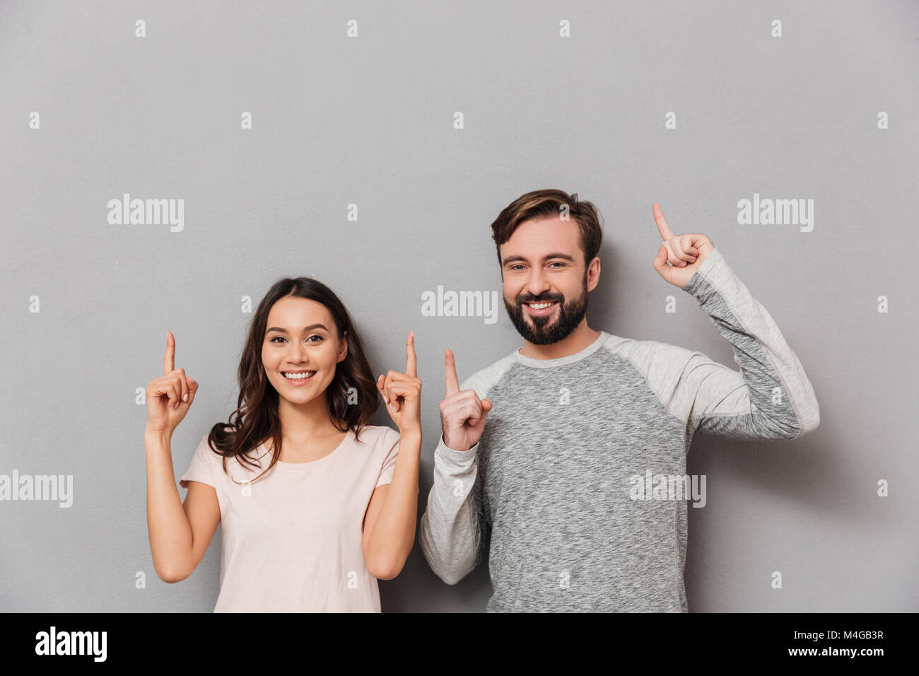 Portrait of a cheerful young couple pointing fingers up at copy space ...