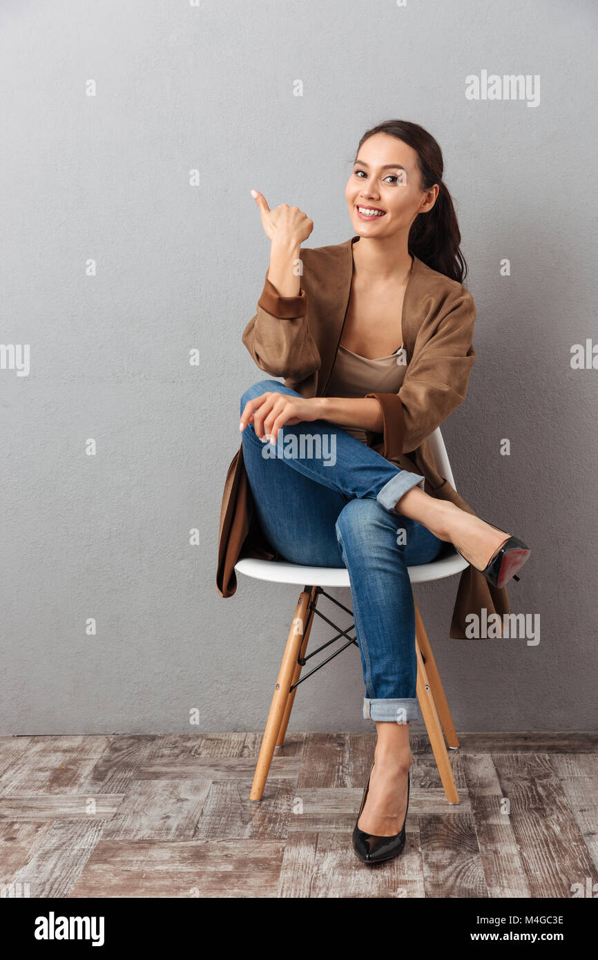 Portrait of a smiling casual asian woman sitting on a chair and ...