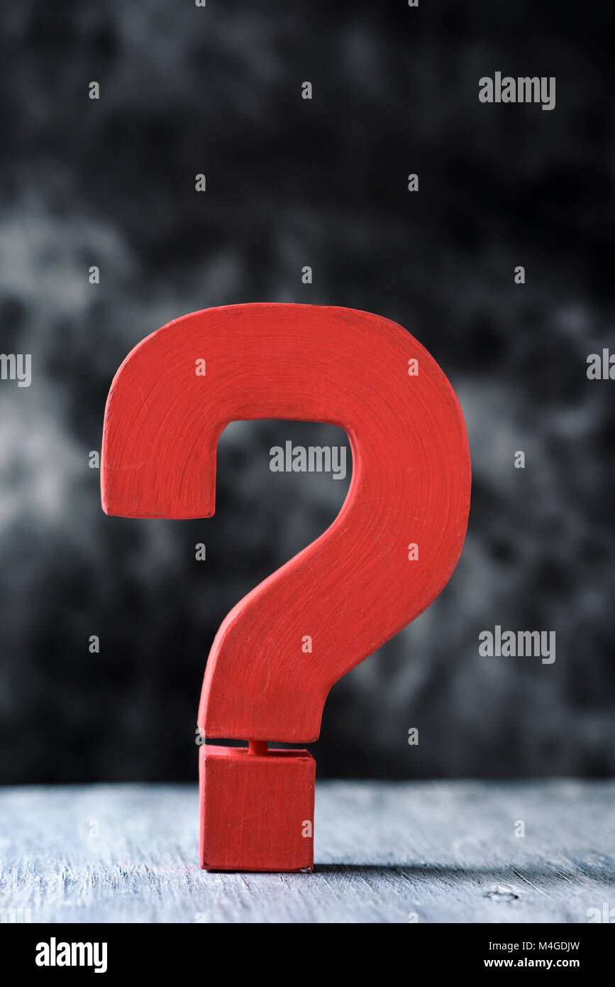 a red three-dimensional question mark on a gray rustic wooden surface ...