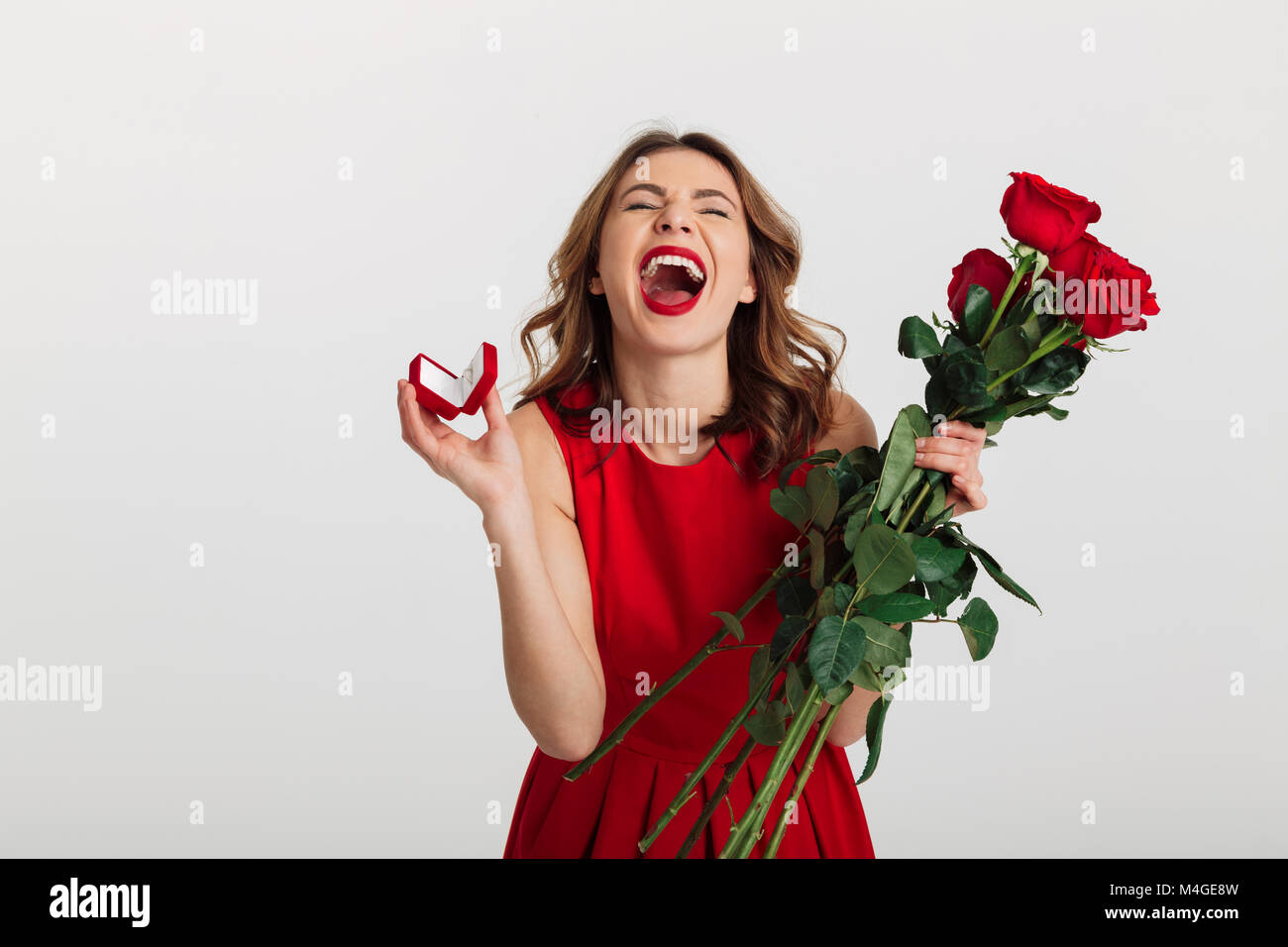 Portrait of an excited young woman dressed in red dress holding box ...