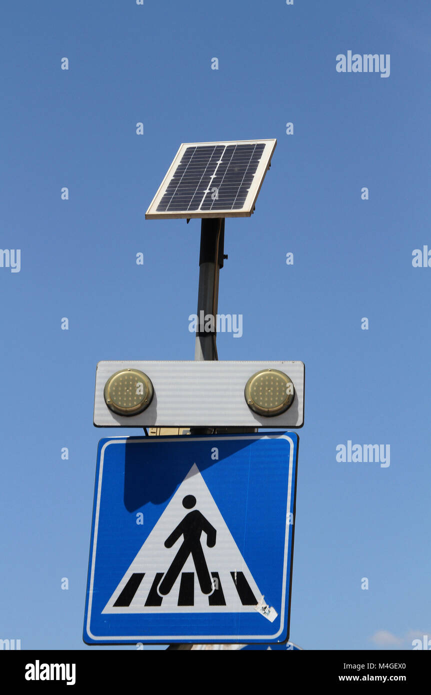 Solar panel with pedestrian crossing lights and sign against blue sky ...