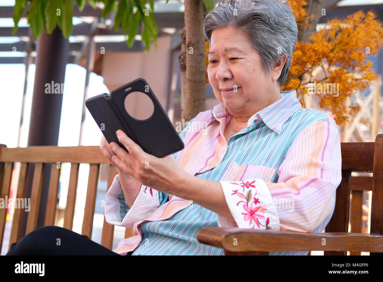 asian elder woman holding mobile phone in garden. elderly female ...