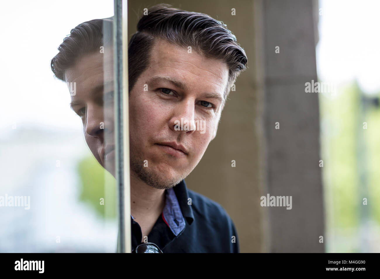 Man posing in front of glass window reflecting his image. Close up ...