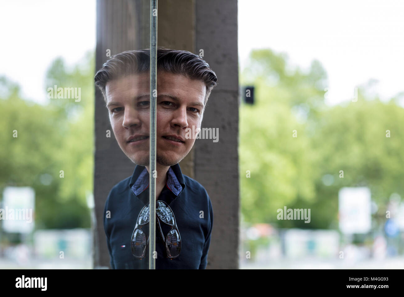 Man posing in front of glass window reflecting his image. Close up ...