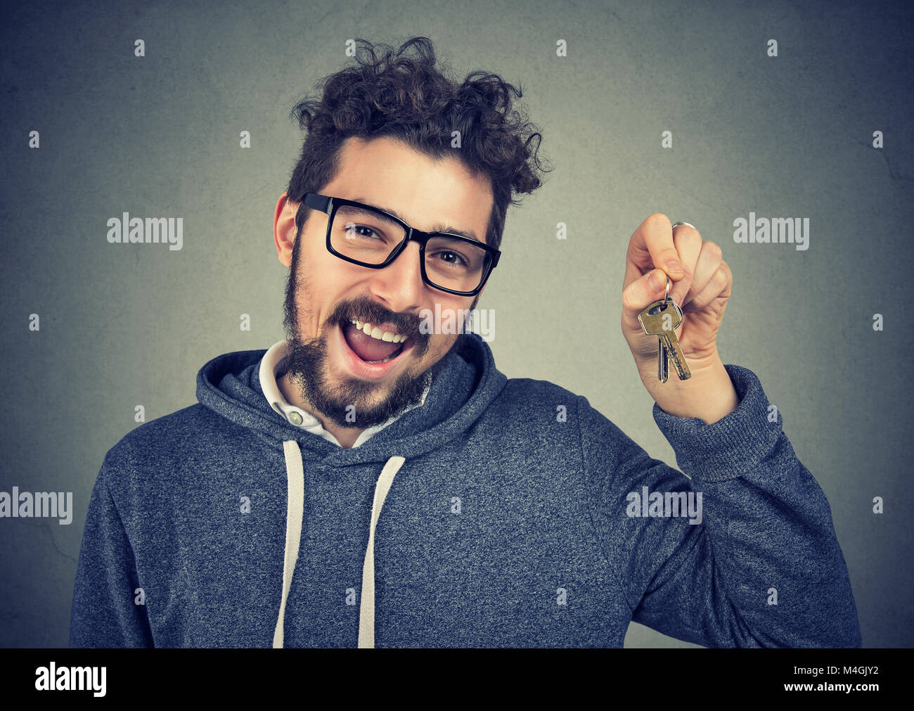 Young cheerful man in glasses boasting with key from new flat smiling ...