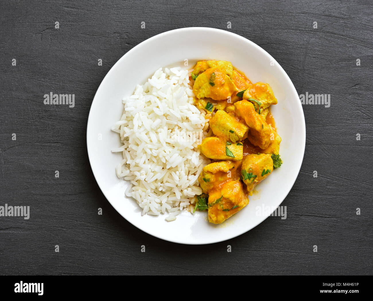 Chicken curry with rice on plate over black stone background. Top view ...