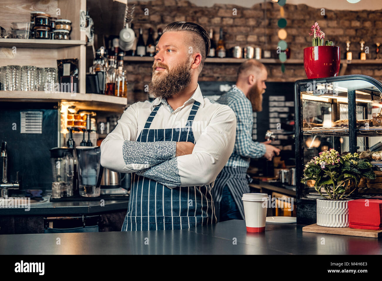Portrait of redhead bearded barista male with crossed arms at bar stand ...