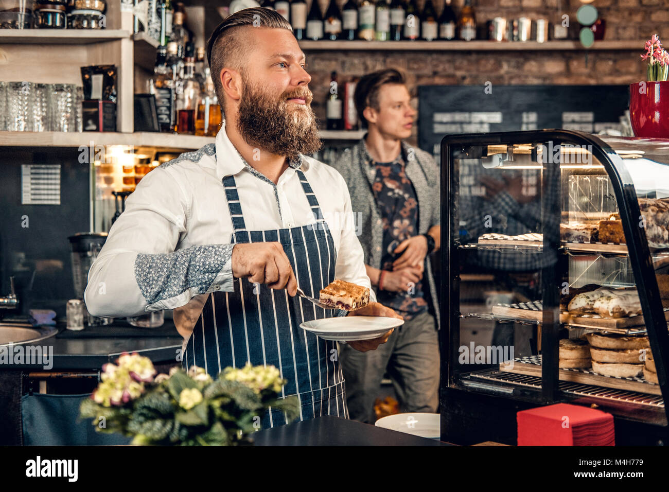 The stylish bearded male holds chocolate cake at the counter in the ...