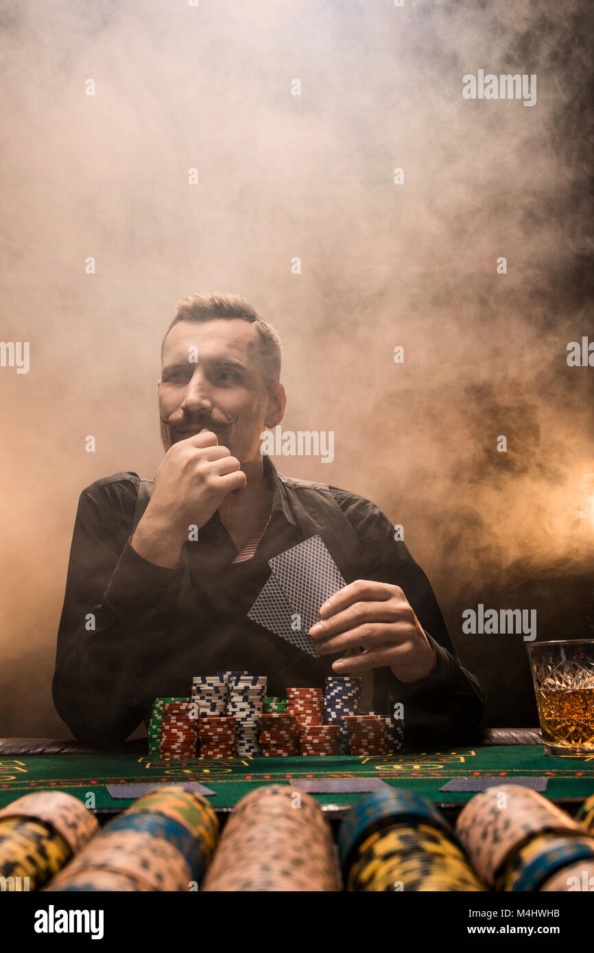 Handsome poker player with two aces in his hands and chips sitting at ...