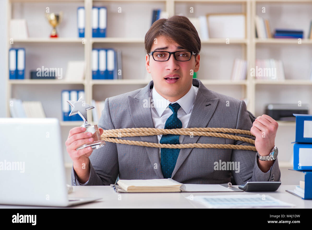 Businessman tied up with rope in office Stock Photo - Alamy