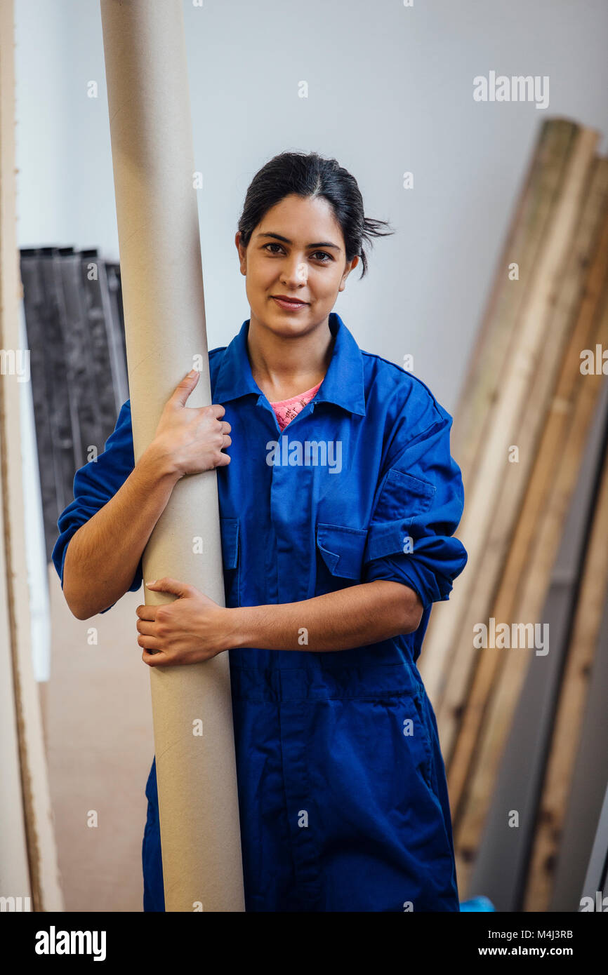 Portrait of a female carpenter at work. She is holding a cardboard tube ...