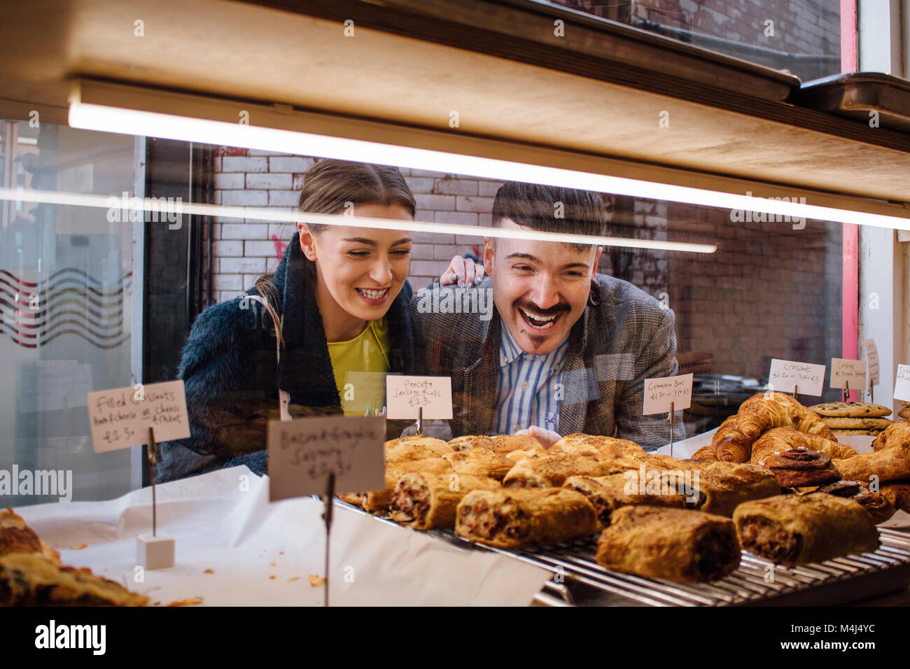 Happy couple are looking into the window of a french bakery. They are ...