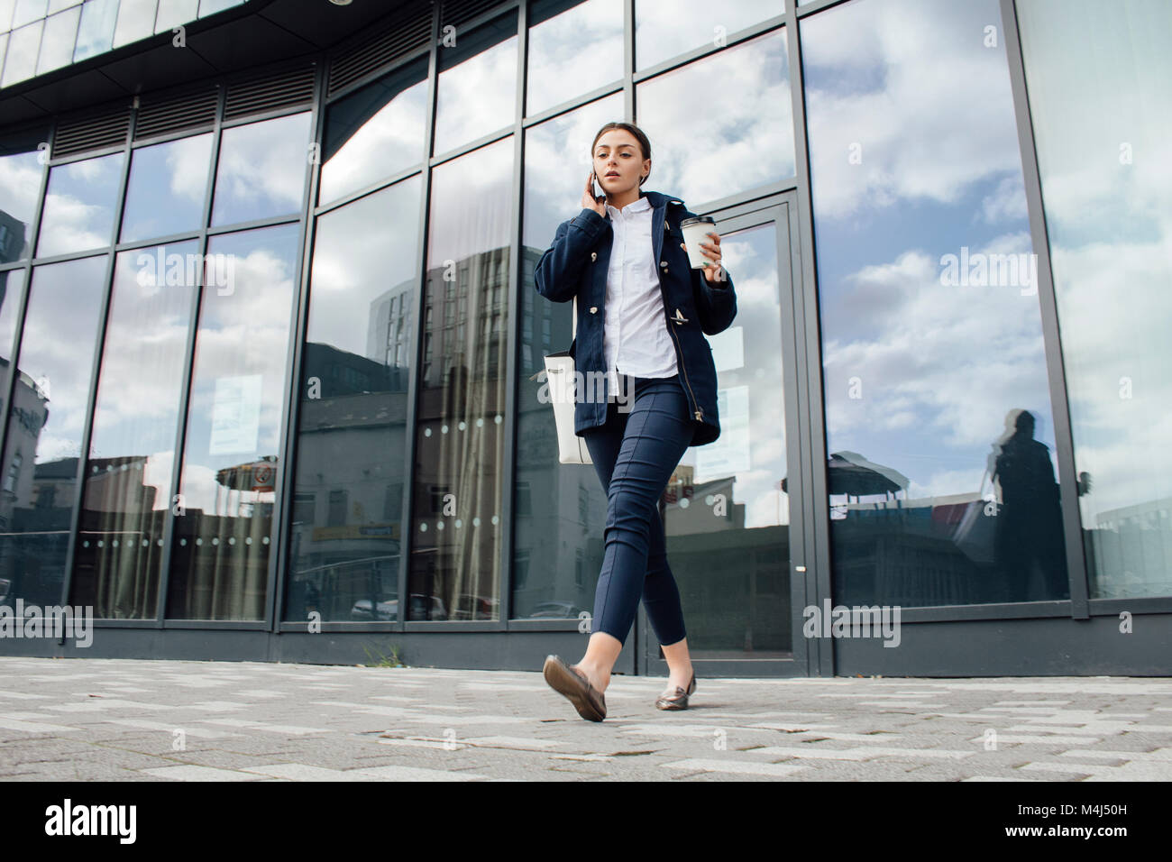 Young businesswoman is leaving her office building with a cup of tea ...