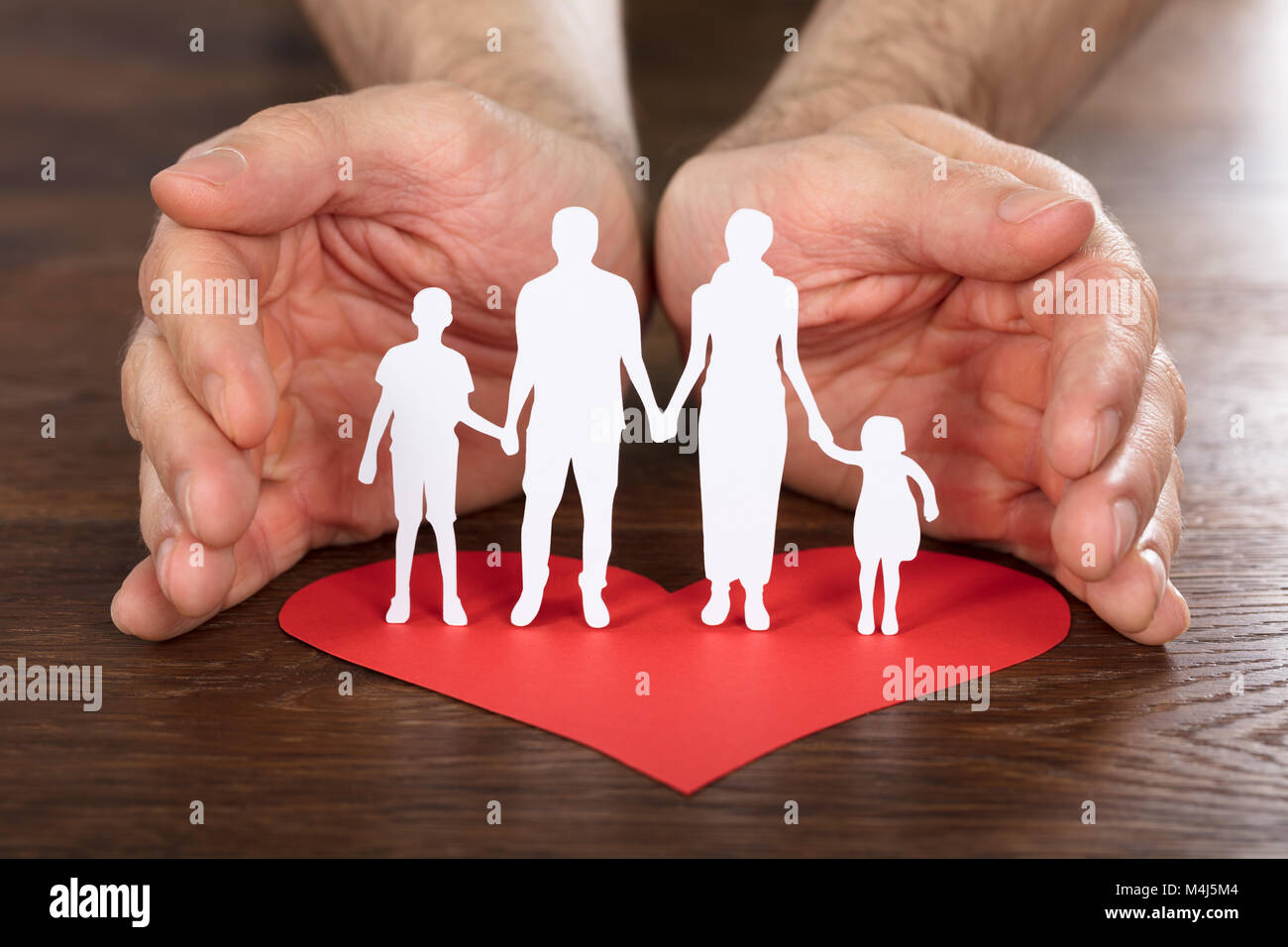 Person Hand Protecting Family Paper Cut With Red Heart On Wooden Desk ...