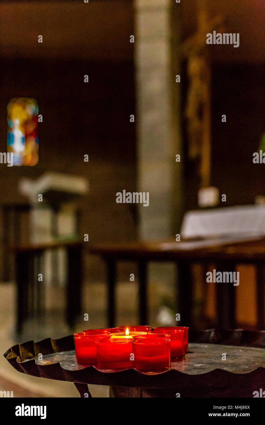 one white candle burning amongst extinguished red ones with Crucifix ...