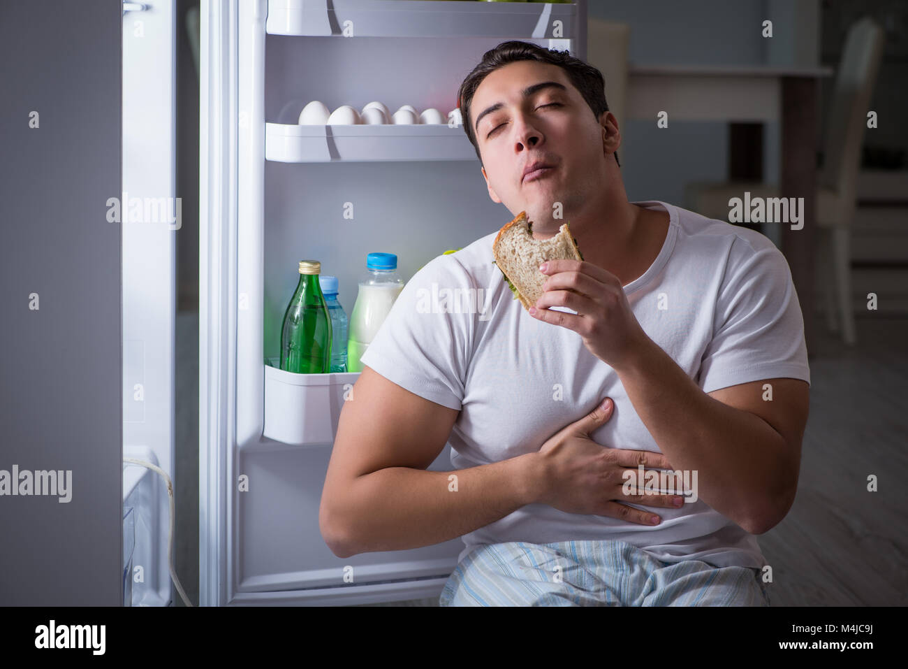 Man at the fridge eating at night Stock Photo - Alamy