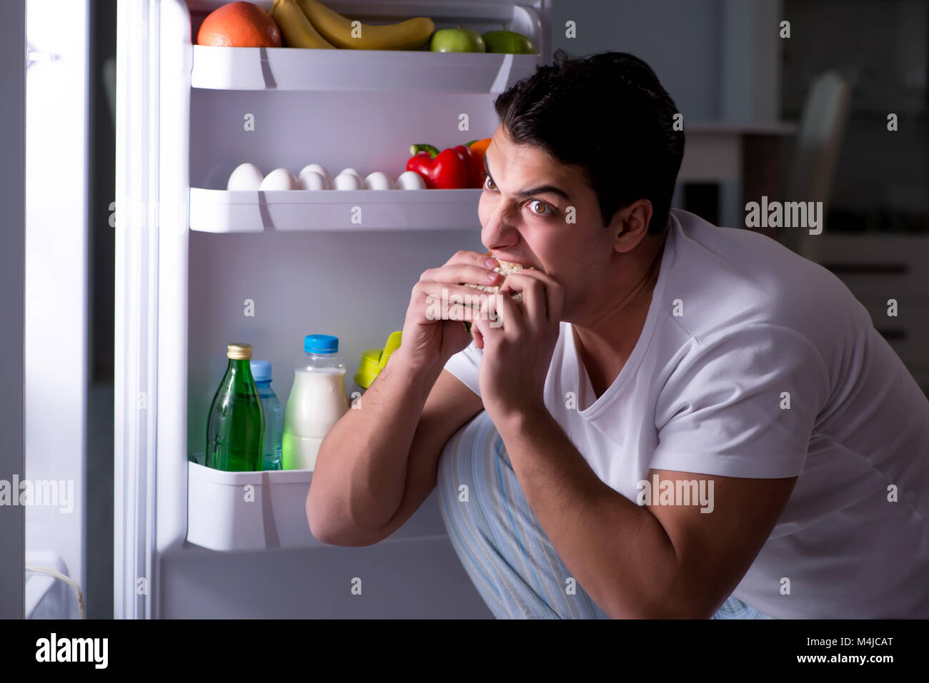 Man at the fridge eating at night Stock Photo - Alamy